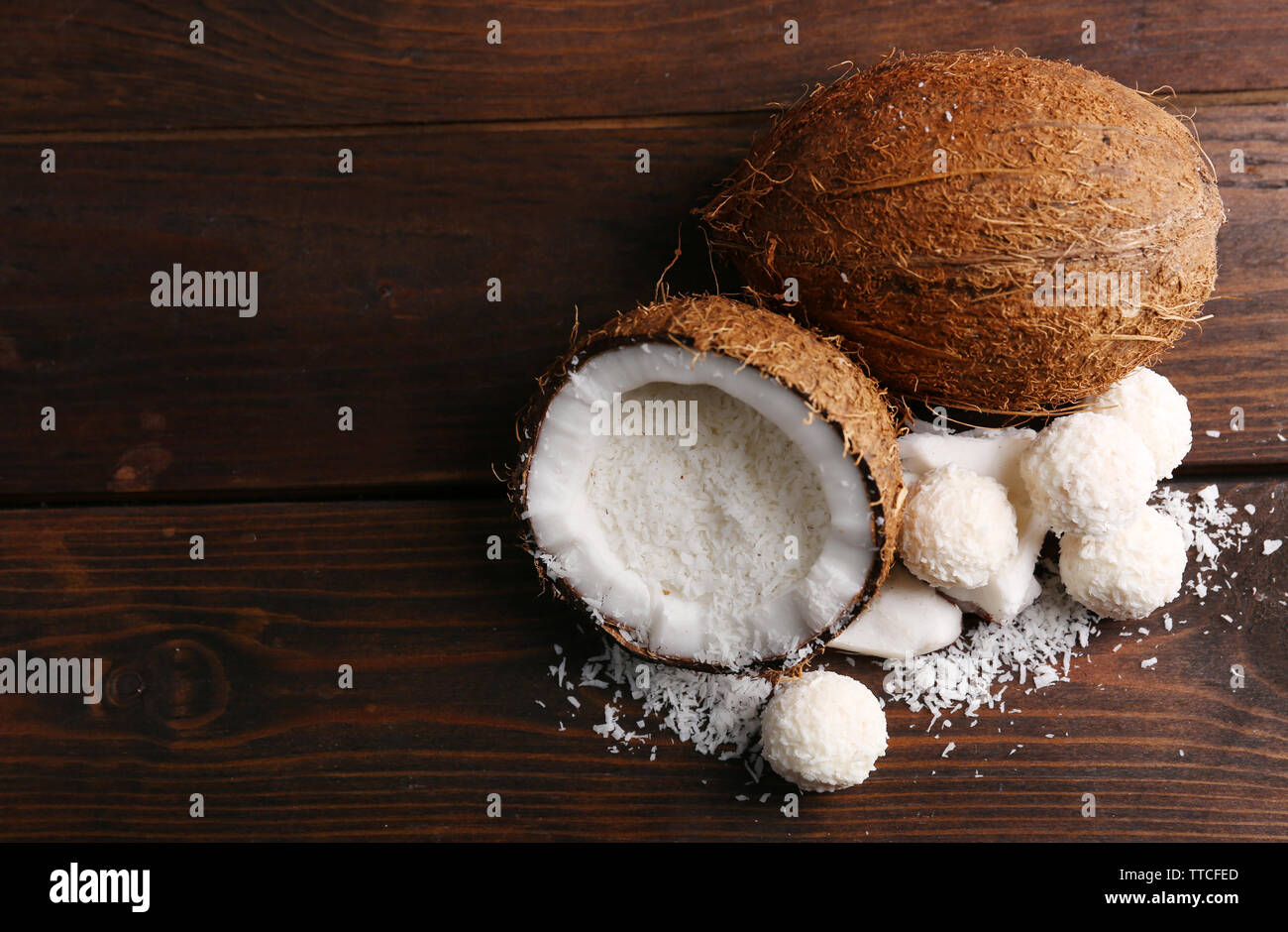 Candies in coconut flakes and fresh coconut on dark wooden background ...