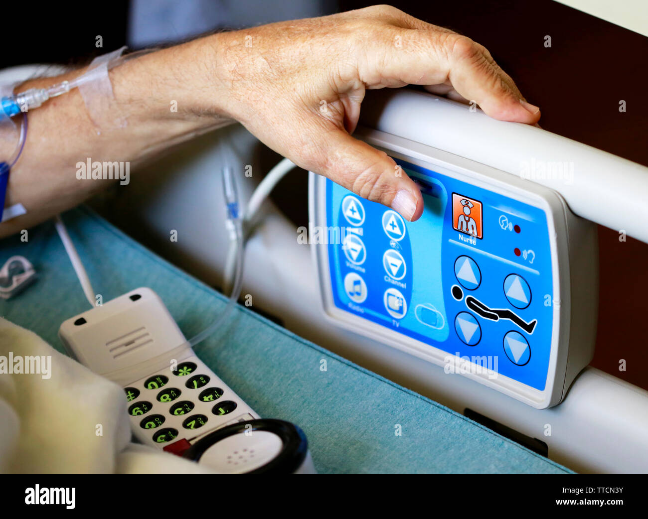 Hospital patient's hand with IV on remote control adjusting the bed ...