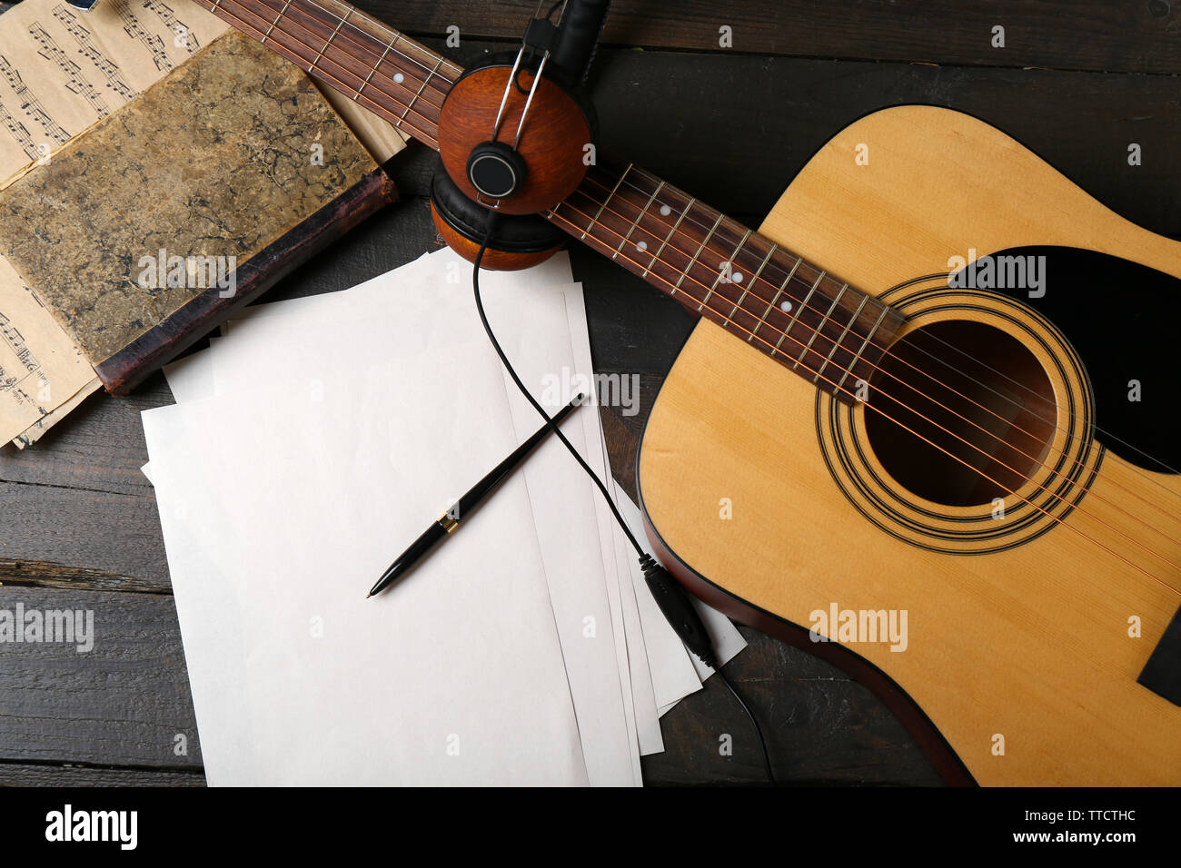 Acoustic guitar, headphones, musical notes and white papers on wooden ...