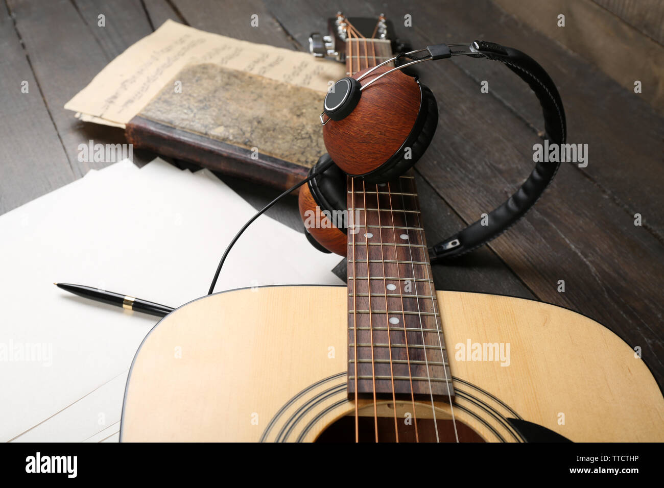 Acoustic guitar, headphones, musical notes and white papers on wooden ...