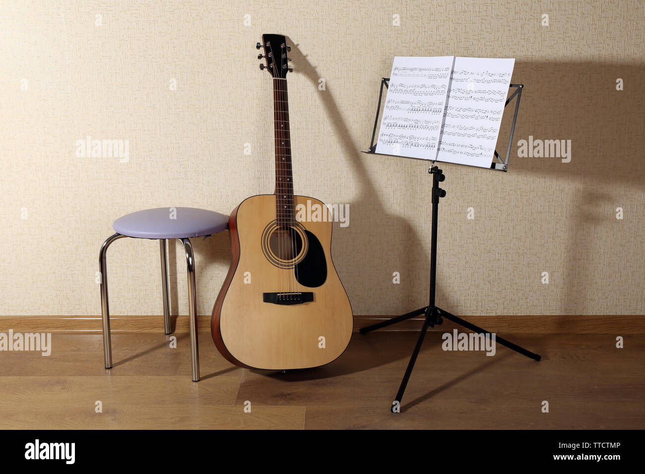 Acoustic guitar propped on wall with stool and musical notes holder in ...