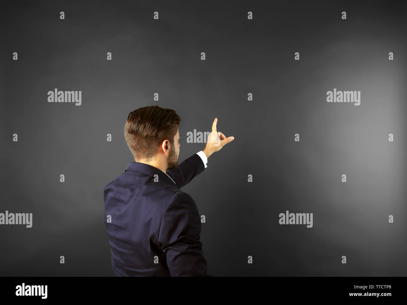 Back view of Caucasian young man in navy blue suit pointing on dark ...