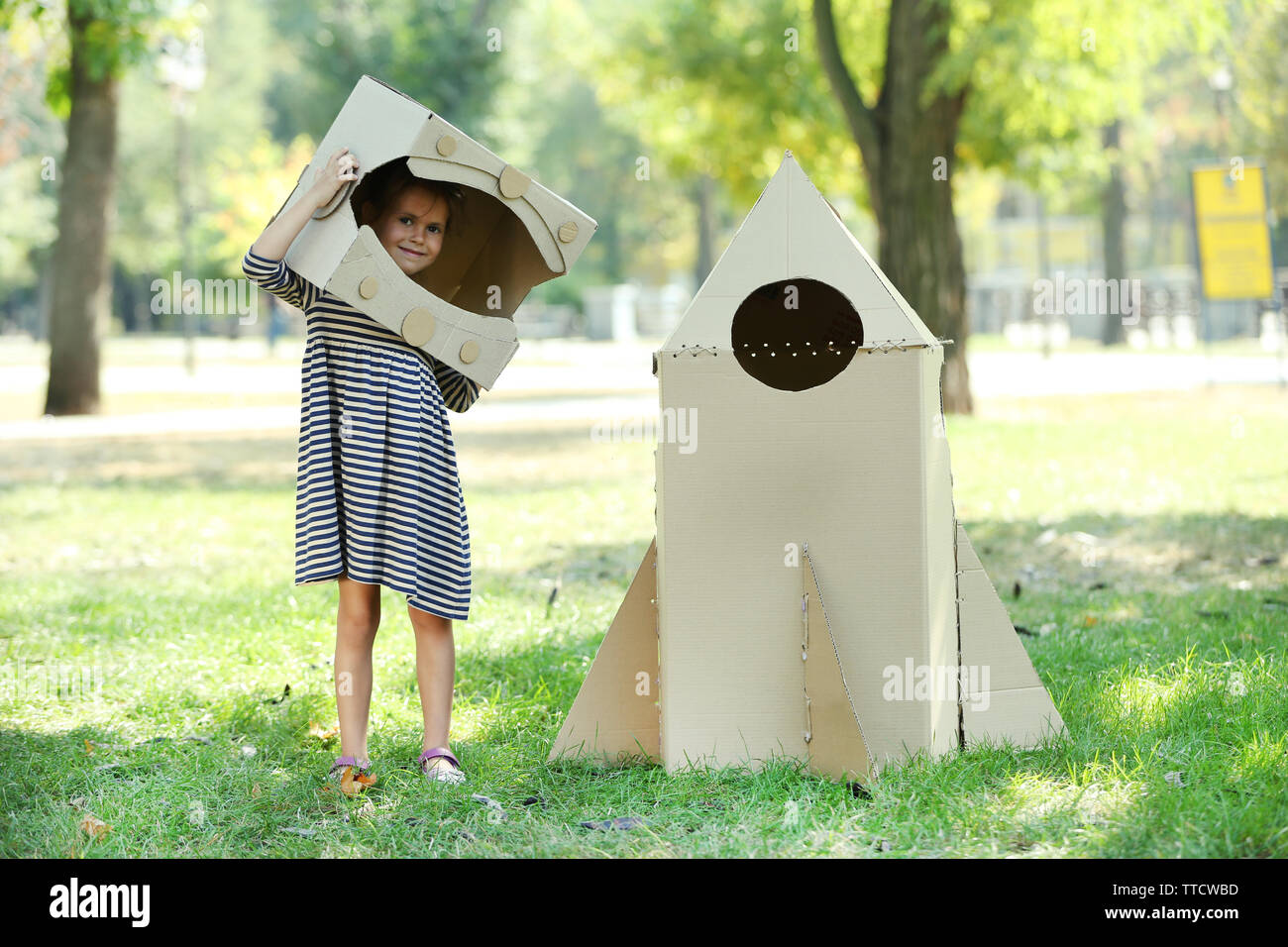 Pretty little girl in box helmet standing near carton rocket in the ...