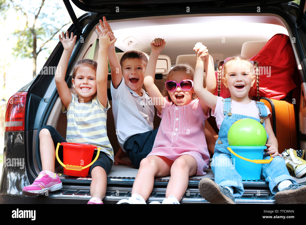 Three adorable girls and boy sit on a car trunk and laughing Stock ...