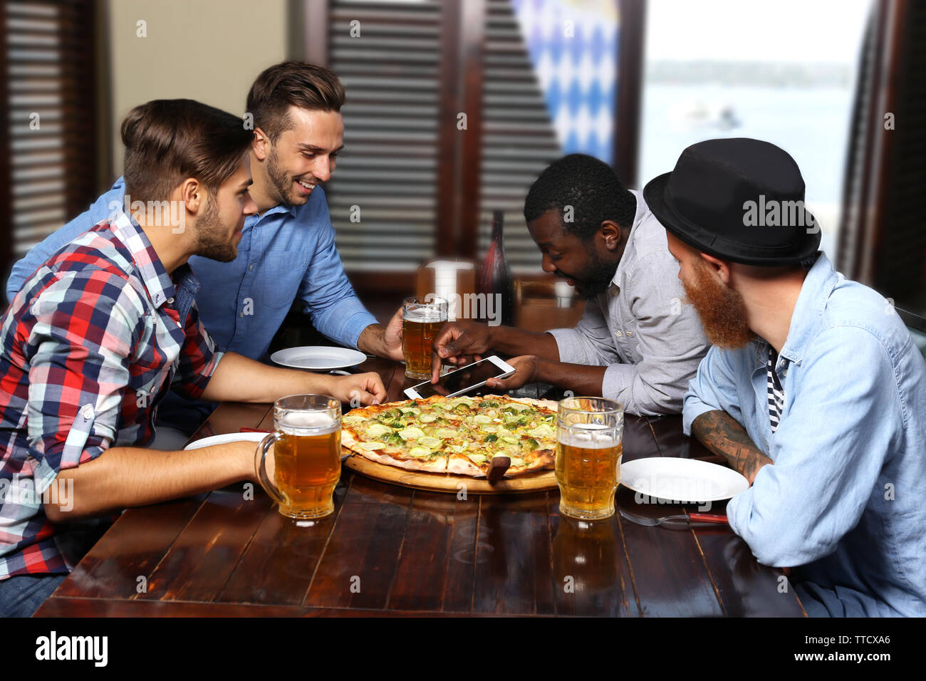 Young men drinking beer and talking in cafe Stock Photo - Alamy