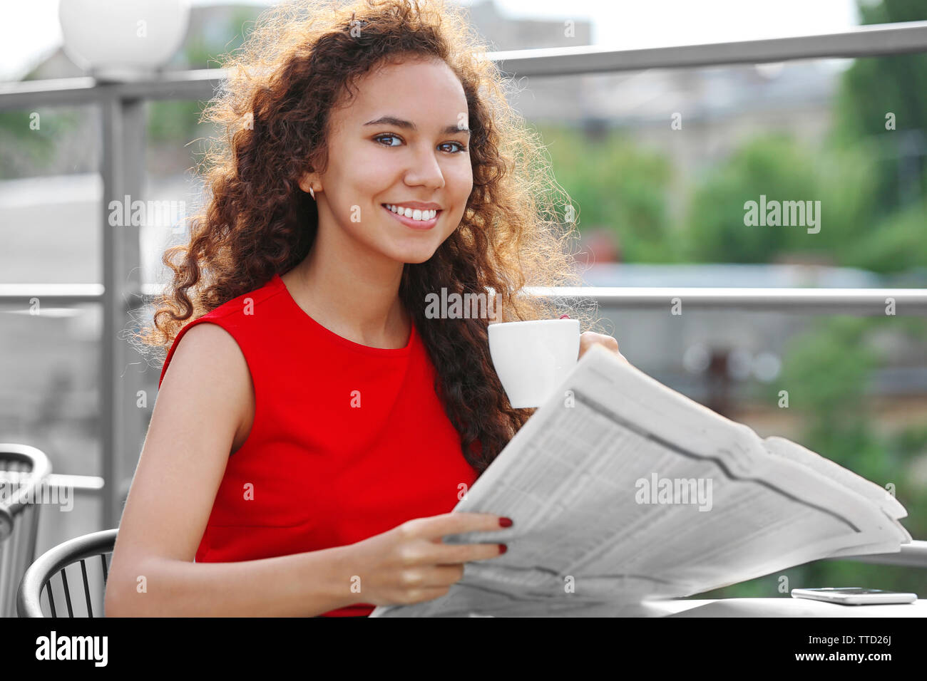 Portrait of young pretty woman in red dress reading newspaper at summer ...