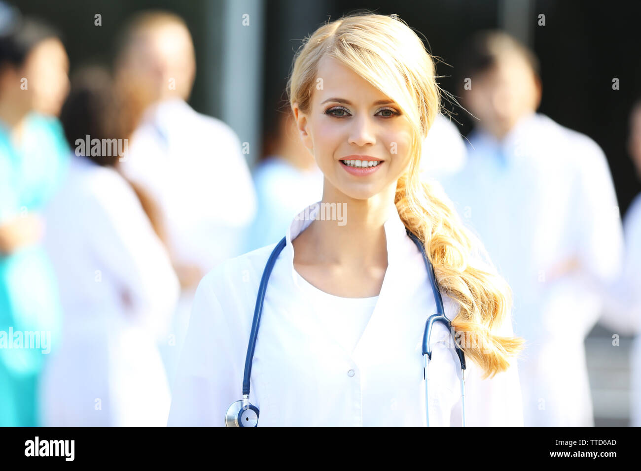 Beautiful smart woman doctor standing against blurred group of medics ...