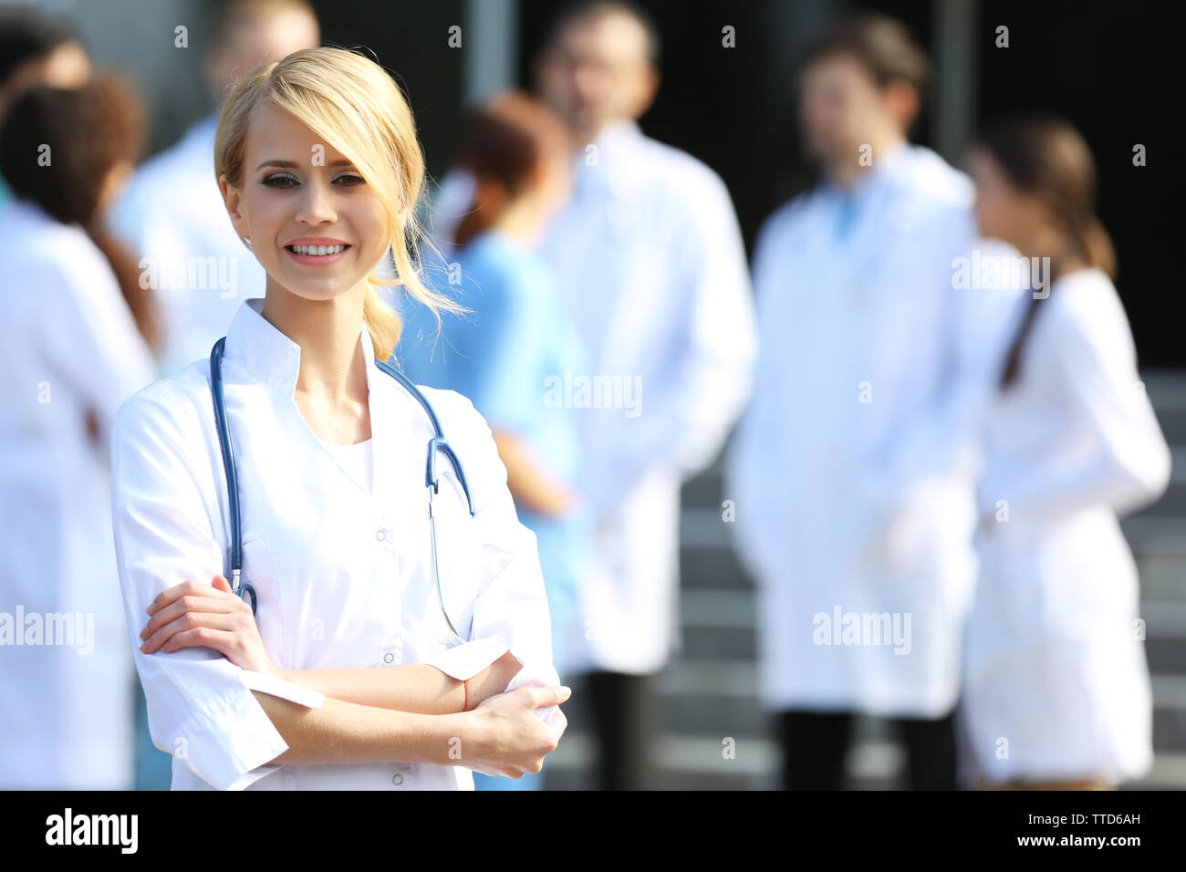 Beautiful smart woman doctor standing against blurred group of medics ...