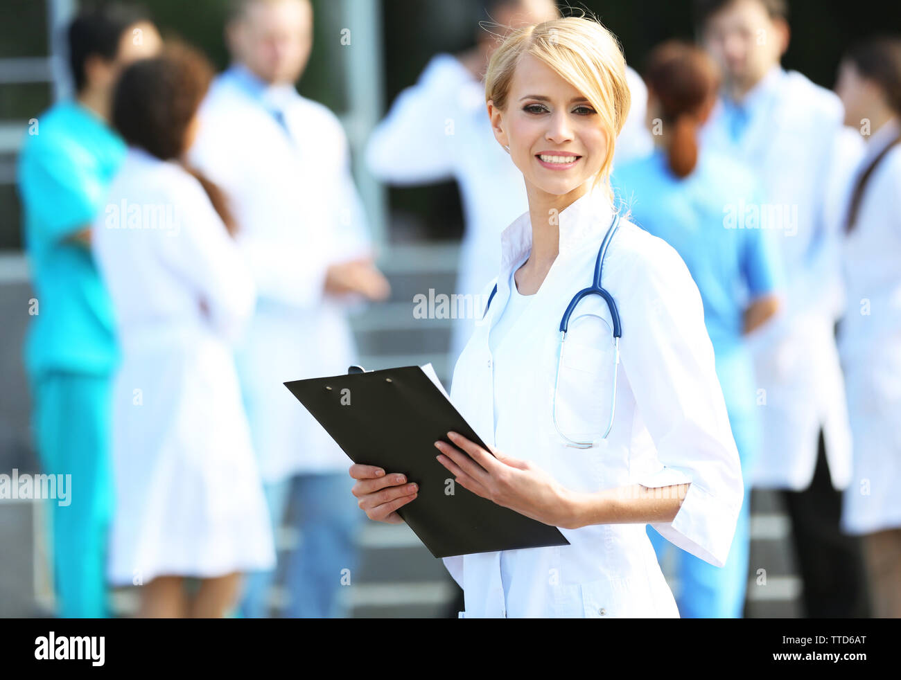 Beautiful smart woman doctor with clipboard in hands standing against ...
