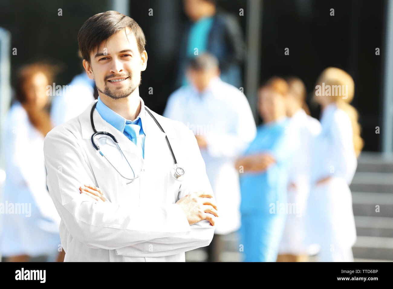 Smiling doctor with medical stuff behind standing against clinic ...