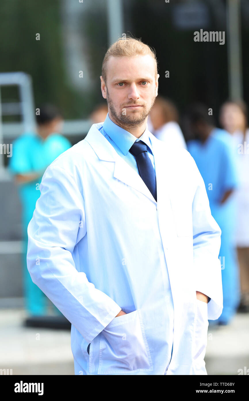 Handsome doctor with medical stuff behind standing against clinic ...