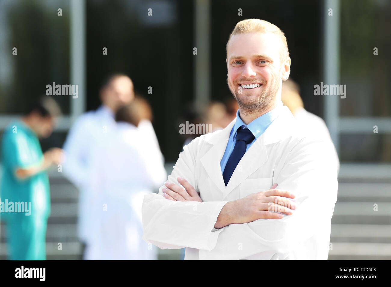 Handsome doctor with medical stuff behind standing against clinic ...