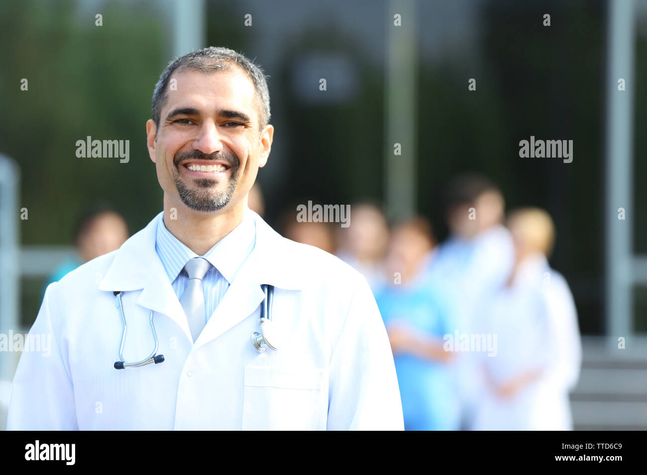 Happy doctor with medical stuff behind standing against clinic entrance ...