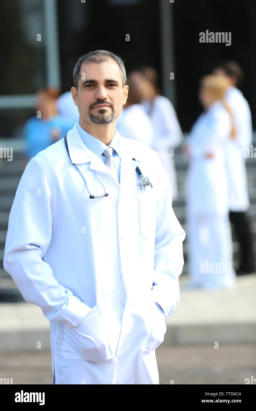 Happy doctor with medical stuff behind standing against clinic entrance ...