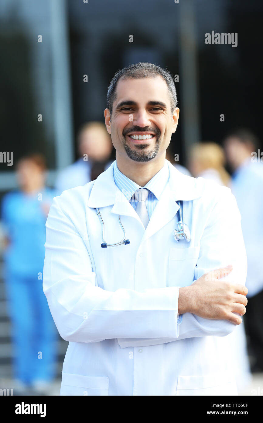 Happy doctor with medical stuff behind standing against clinic entrance ...