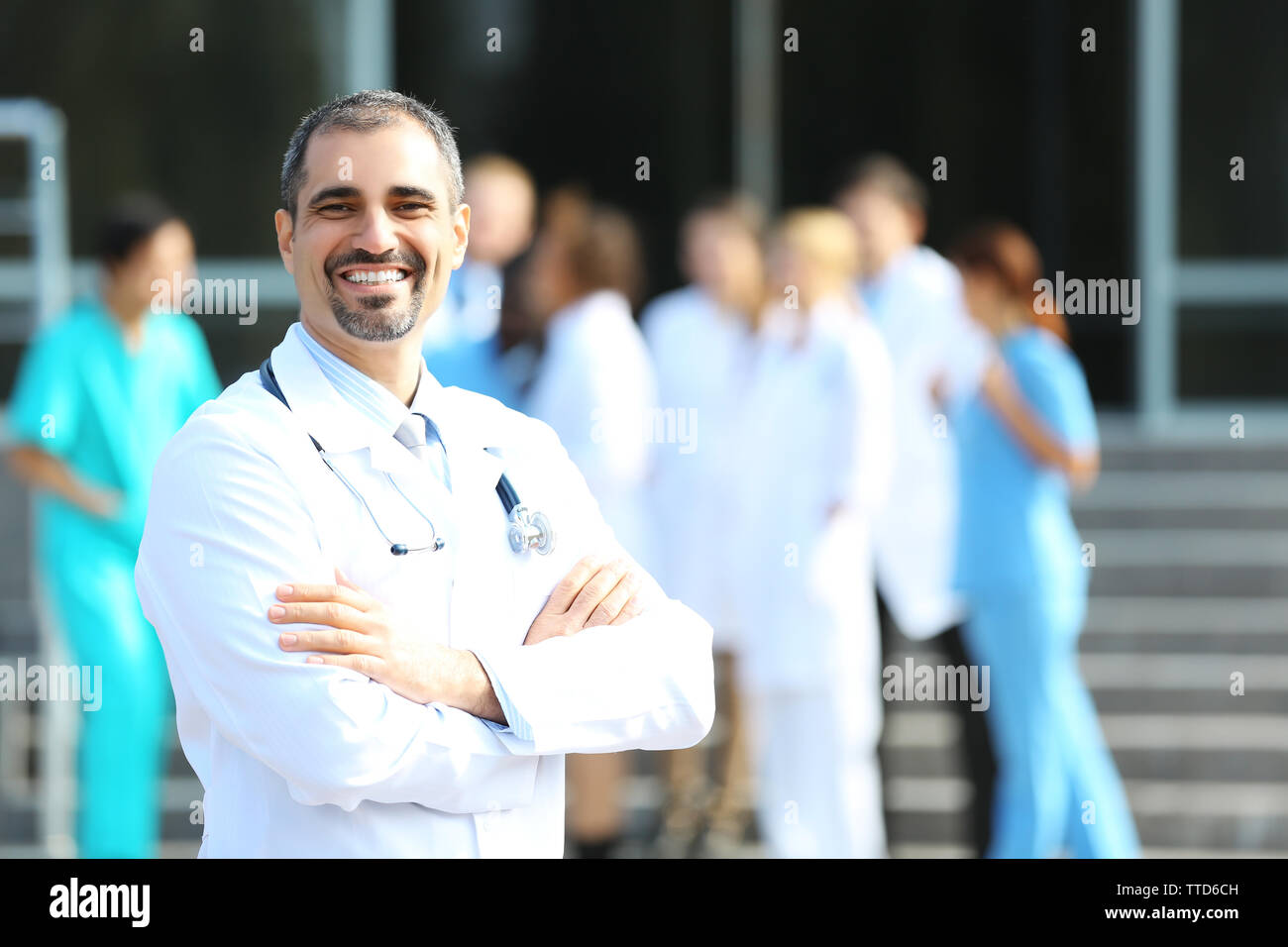 Happy doctor with medical stuff behind standing against clinic entrance ...