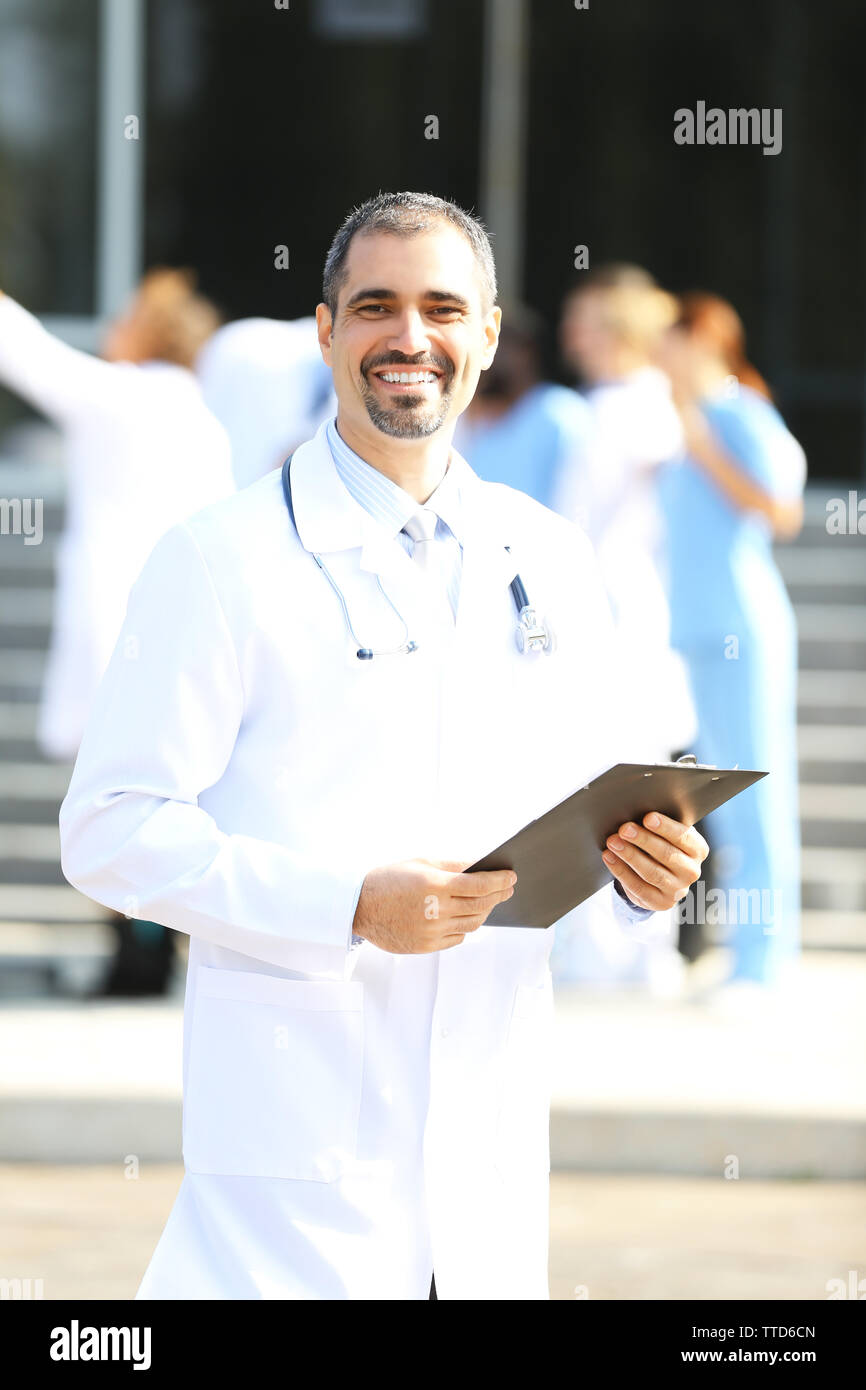 Happy doctor holds clipboard in hands with medical stuff behind ...