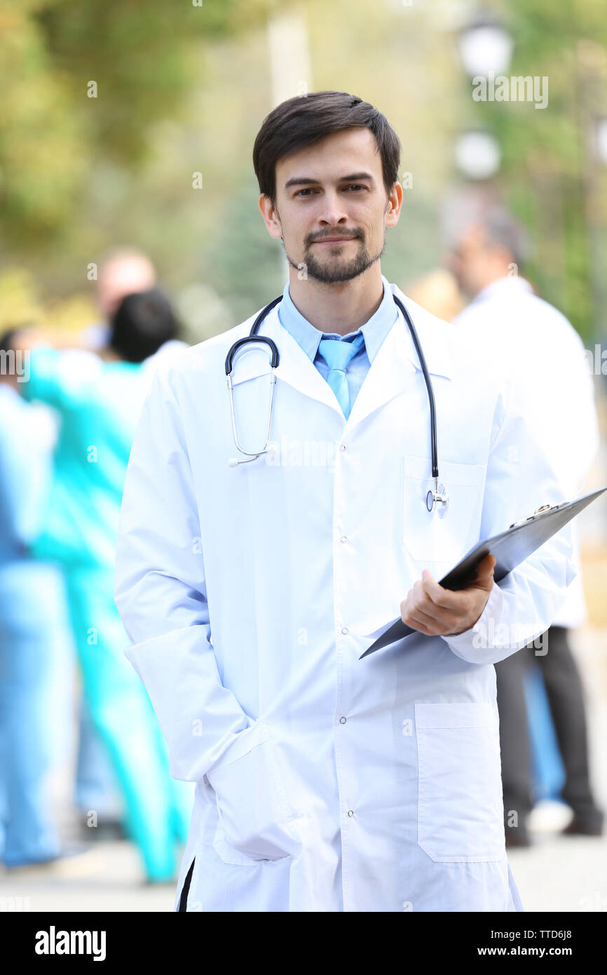 Smiling doctor holds clipboard in hands with medical stuff behind ...