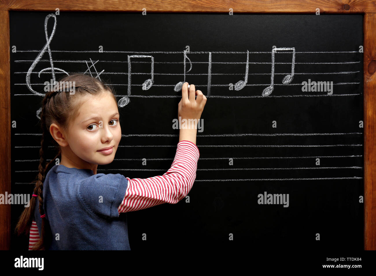 Cute girl writing at the blackboard with musical notes, in the ...