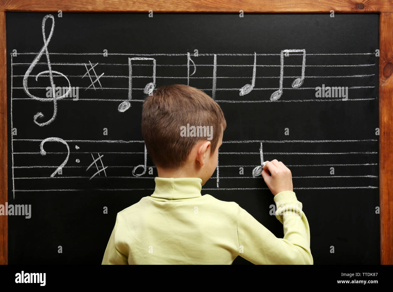 Cute boy writing at the blackboard with musical notes, in the classroom ...