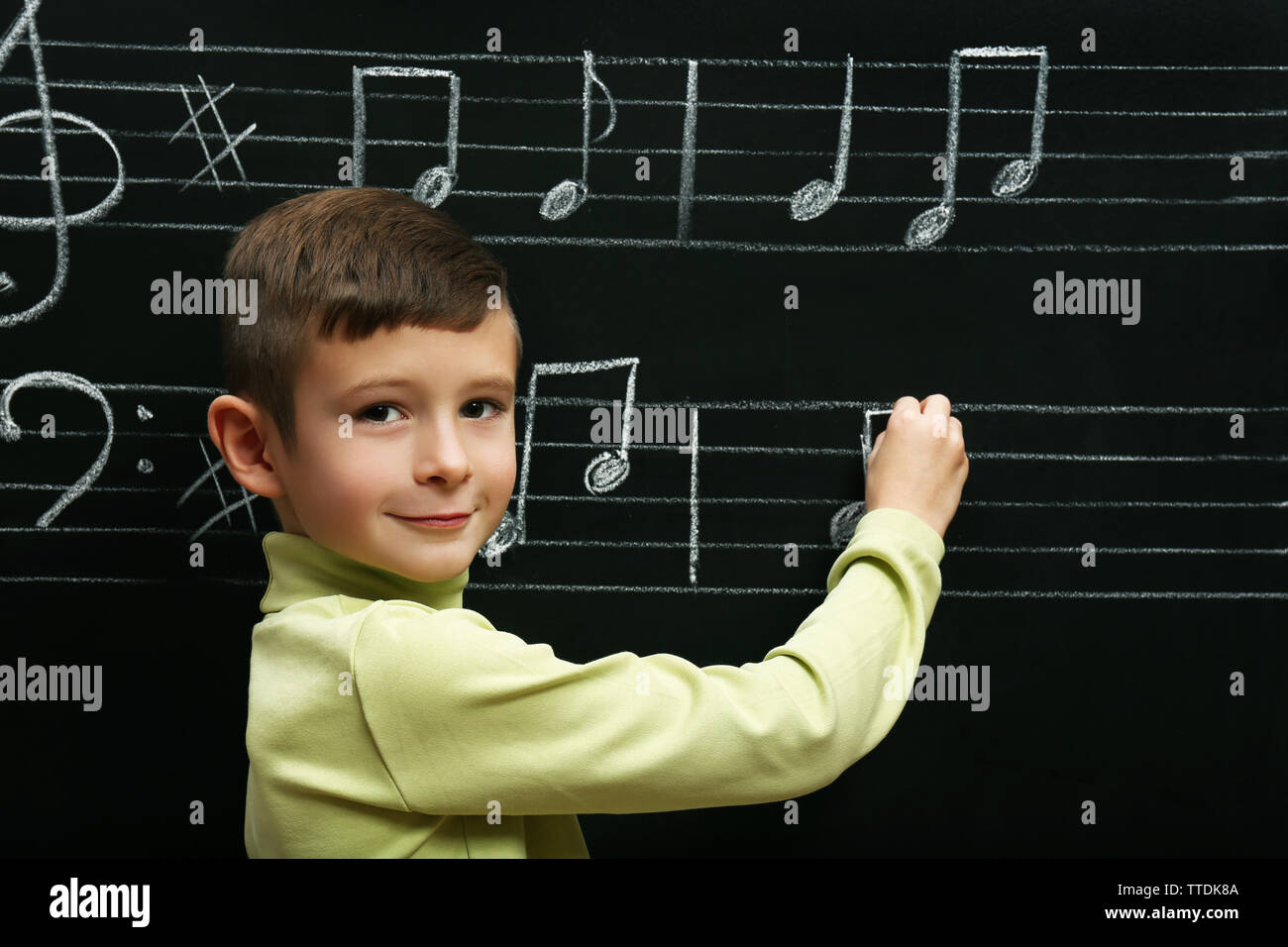 Cute boy writing at the blackboard with musical notes, in the classroom ...