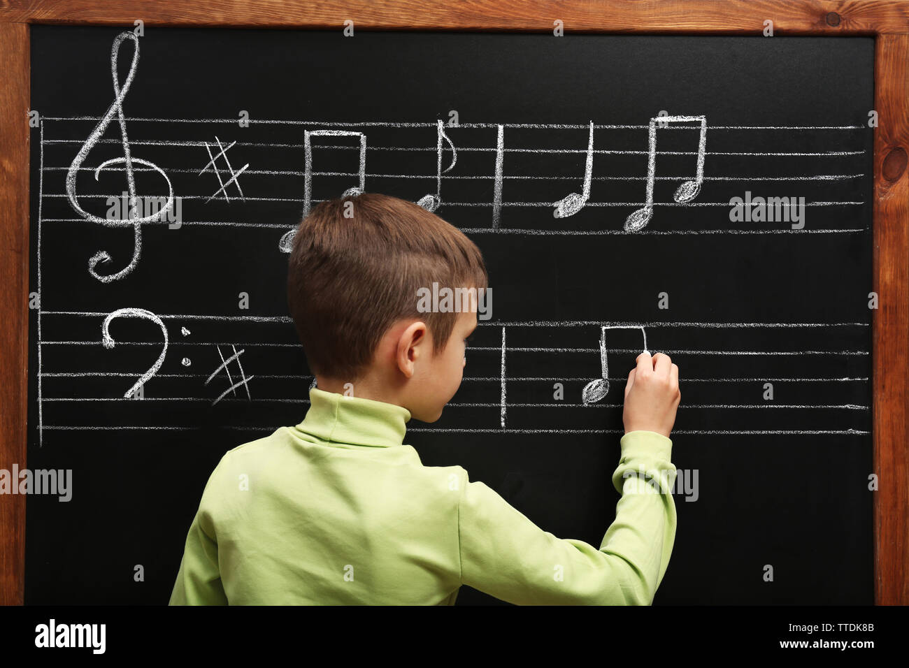 Cute boy writing at the blackboard with musical notes, in the classroom ...