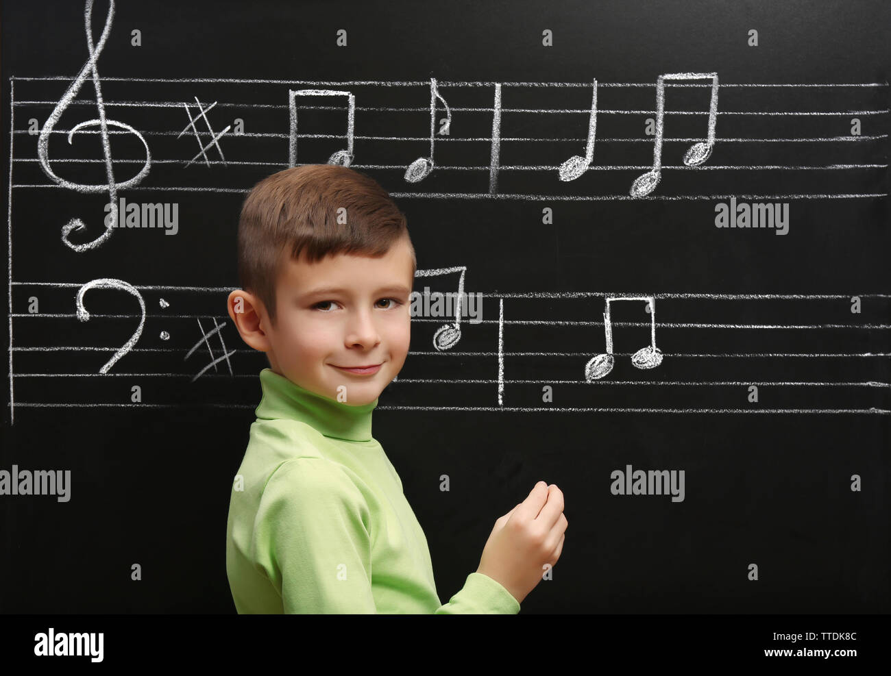 Cute boy writing at the blackboard with musical notes, in the classroom ...