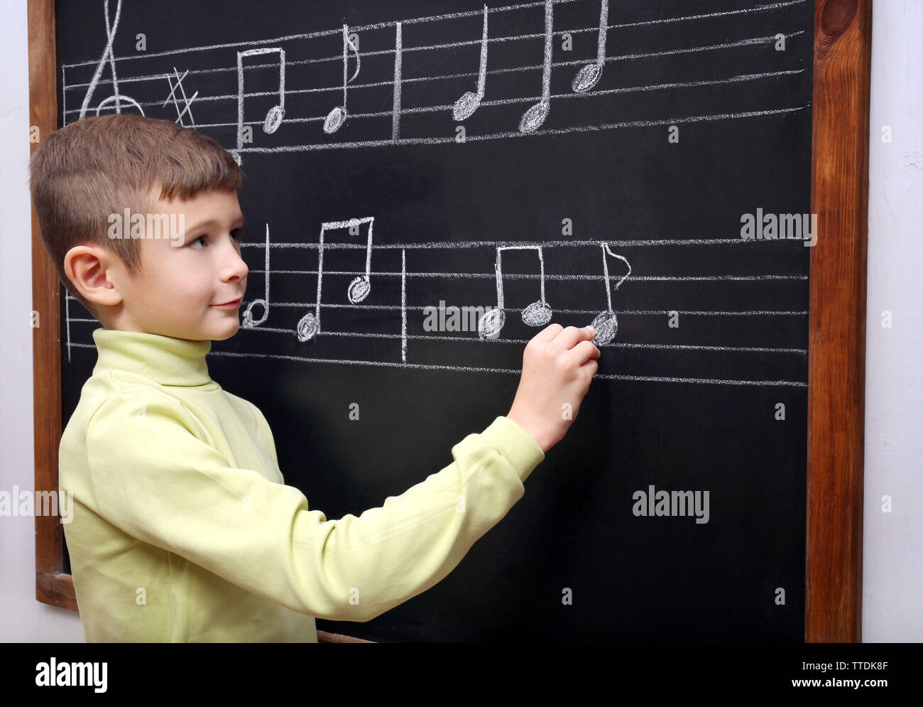 Cute boy writing at the blackboard with musical notes, in the classroom ...
