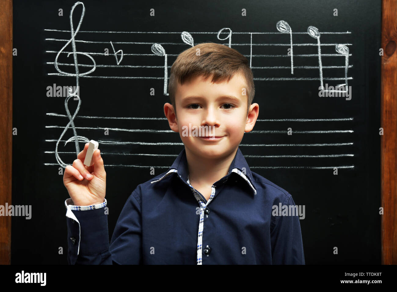 Cute boy standing at the blackboard with musical notes, in the ...