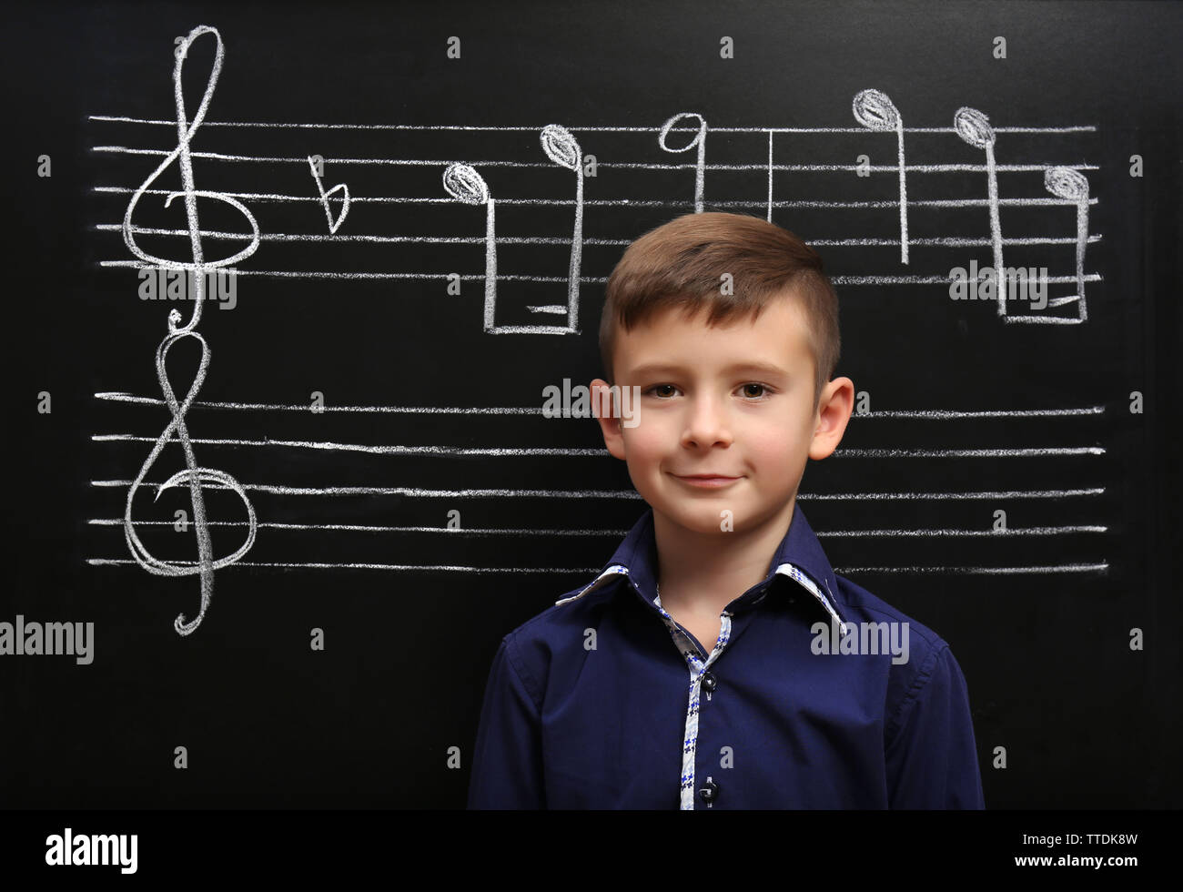 Cute boy standing at the blackboard with musical notes, in the ...