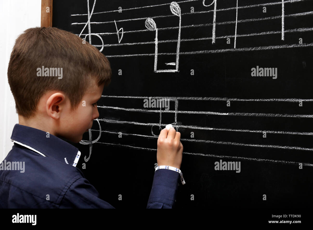 Cute boy writing at the blackboard with musical notes, in the classroom ...