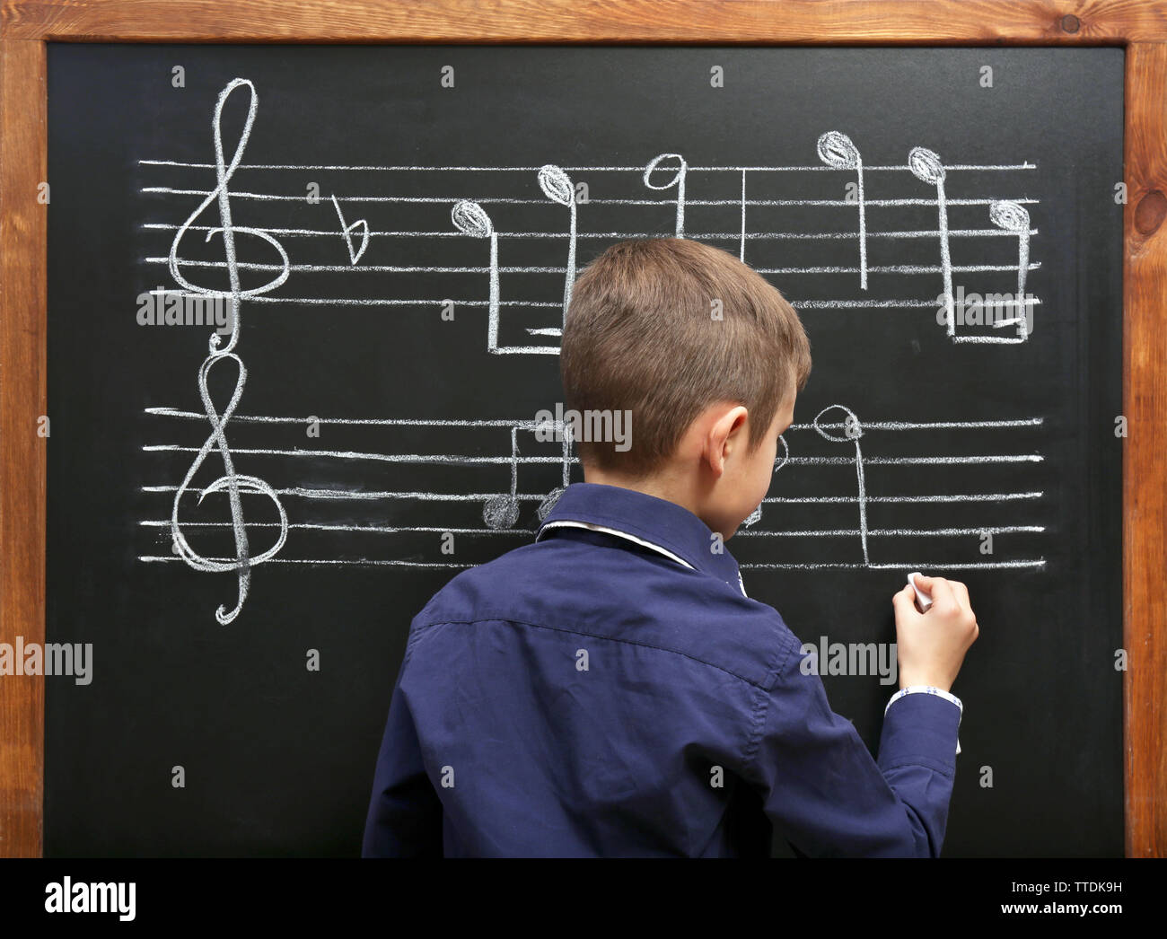Cute boy writing at the blackboard with musical notes, in the classroom ...