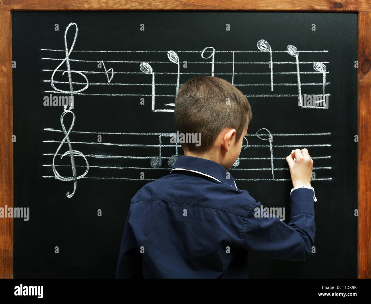 Cute boy writing at the blackboard with musical notes, in the classroom ...