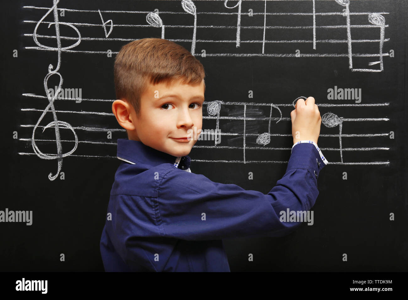 Cute boy writing at the blackboard with musical notes, in the classroom ...