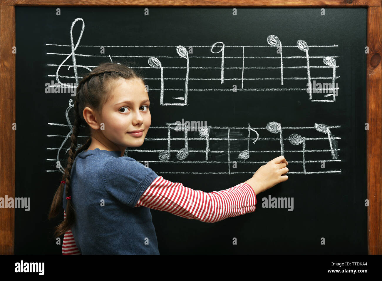 Cute girl writing at the blackboard with musical notes, in the ...