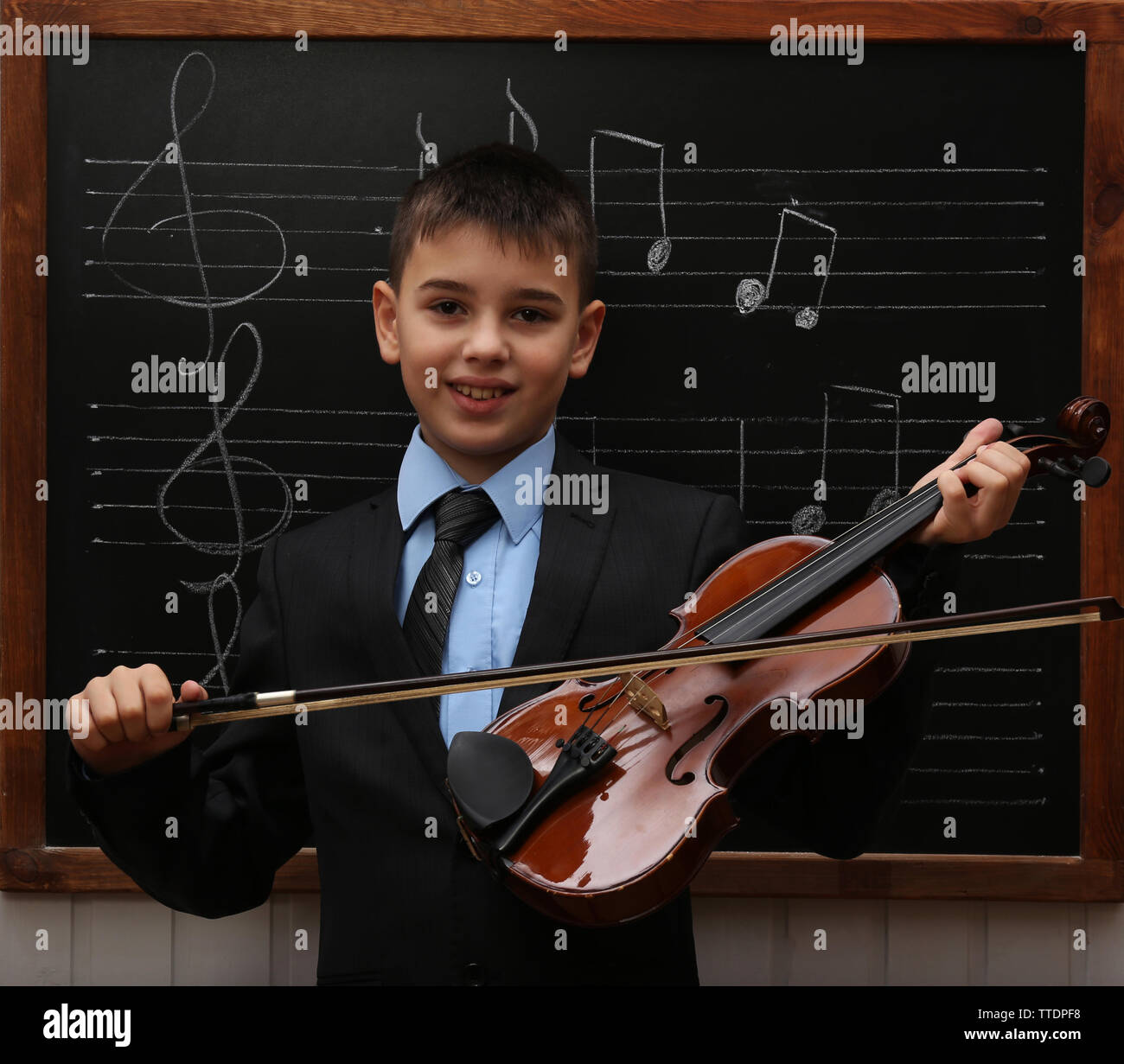 Young cute schoolboy holding the violin at the blackboard with musical ...