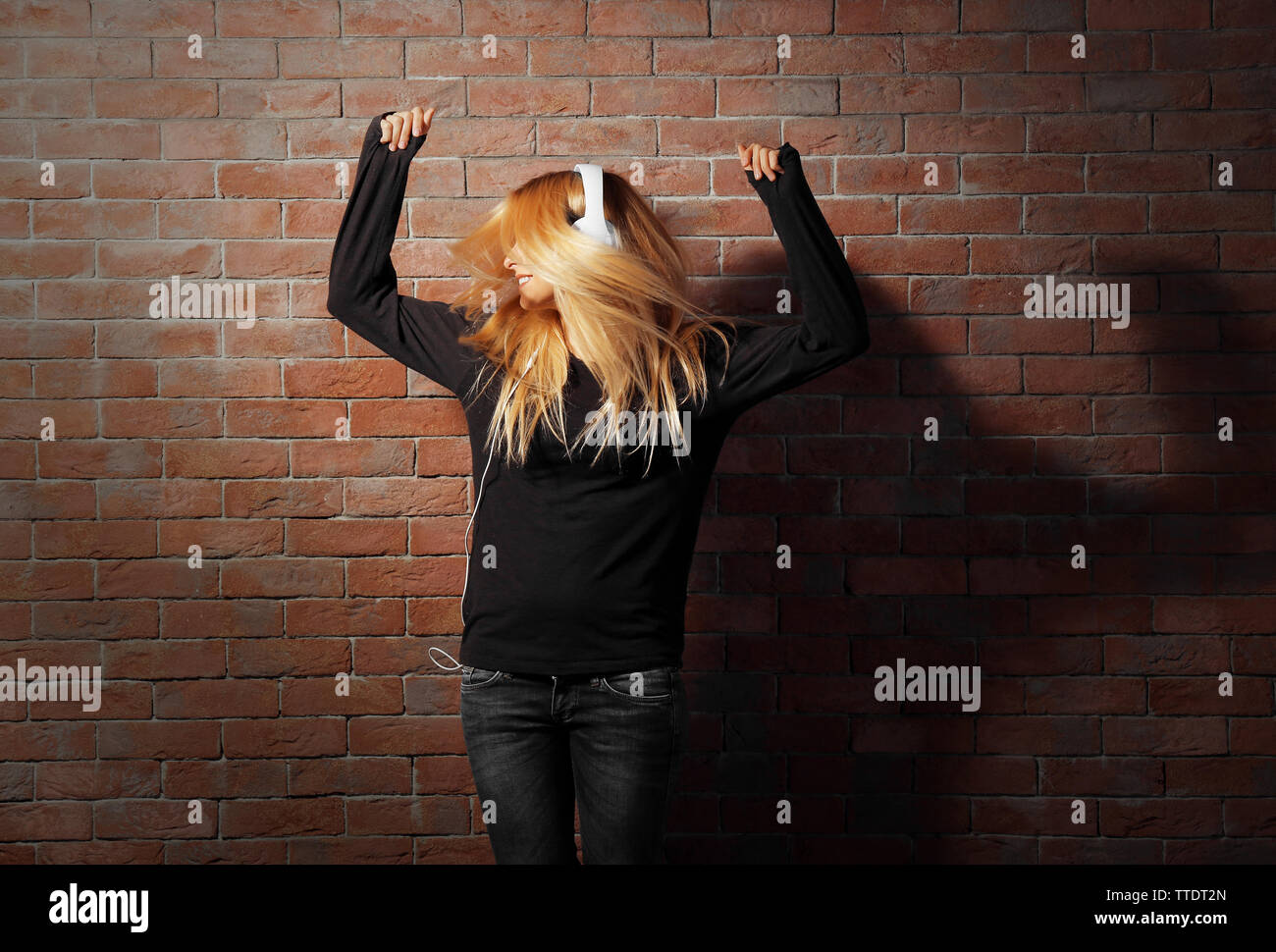 Young woman standing at the brick wall and listening to music Stock ...