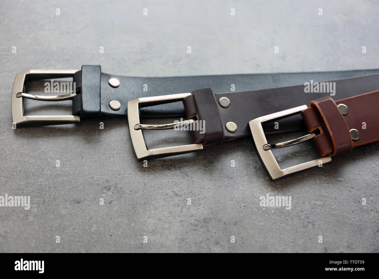 Leather belts with buckles on gray background Stock Photo - Alamy