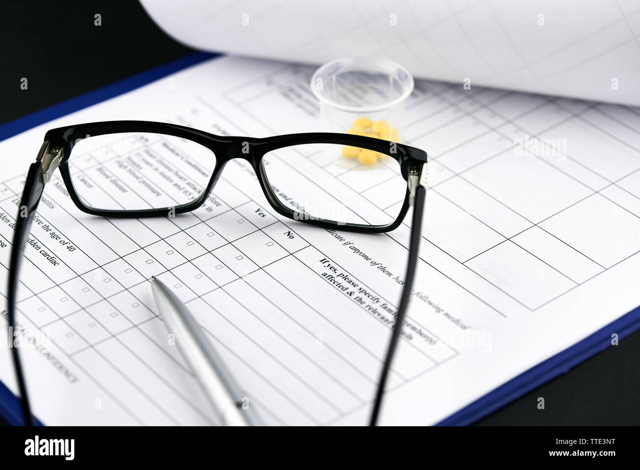 Glasses, yellow pills in graduated glass and pen on medical ...
