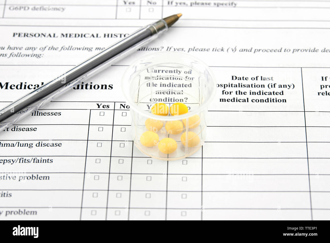 Yellow pills in graduated glass and pen on medical questionnaire form ...