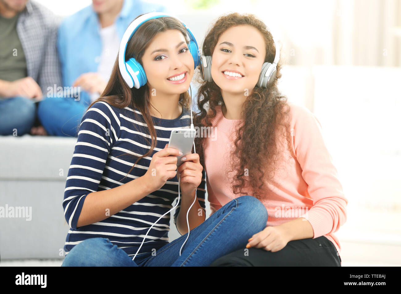 Two teenager girls listening to music with headphones in living room ...