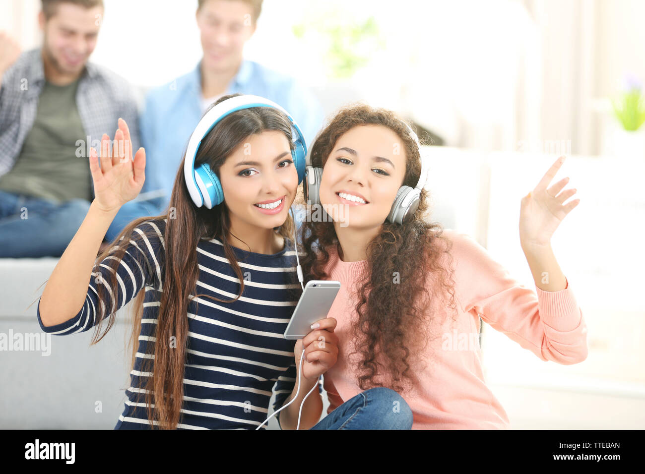 Two teenager girls listening to music with headphones in living room ...