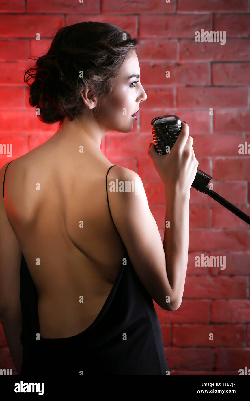 Beautiful brunette singing woman on brick wall background, backside ...