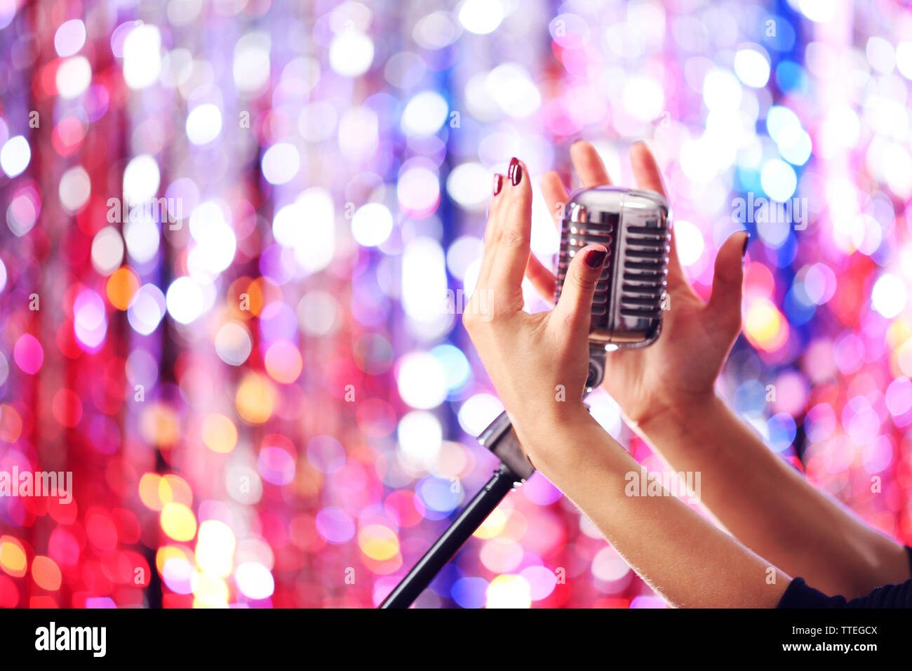 Female hands holding microphone against bright glitter background Stock ...