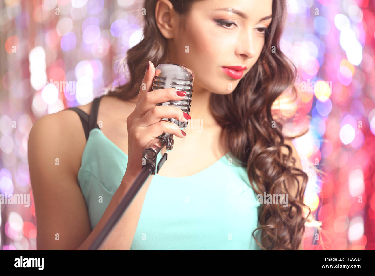 Young cute woman singing against bright glitter background Stock Photo ...