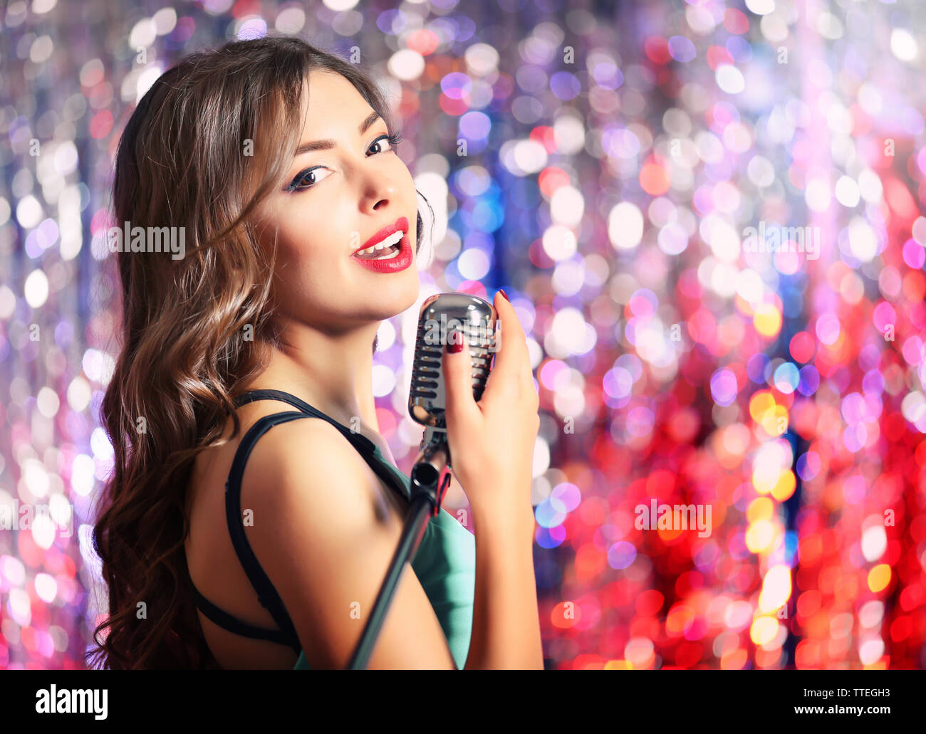 Portrait of beautiful singing woman against bright glitter background ...