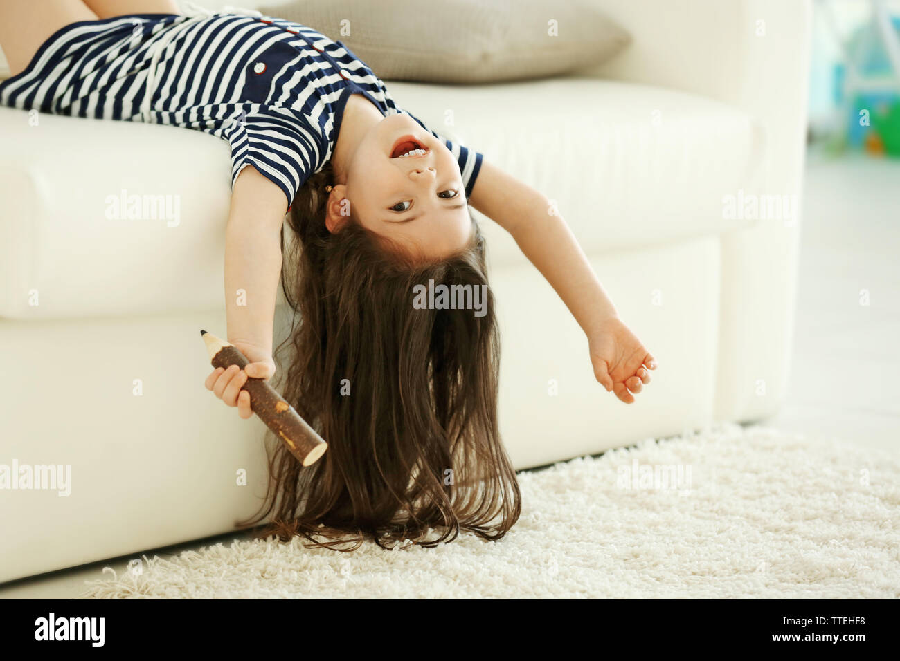 Cute little girl sings in an imagine microphone lying on sofa in the ...