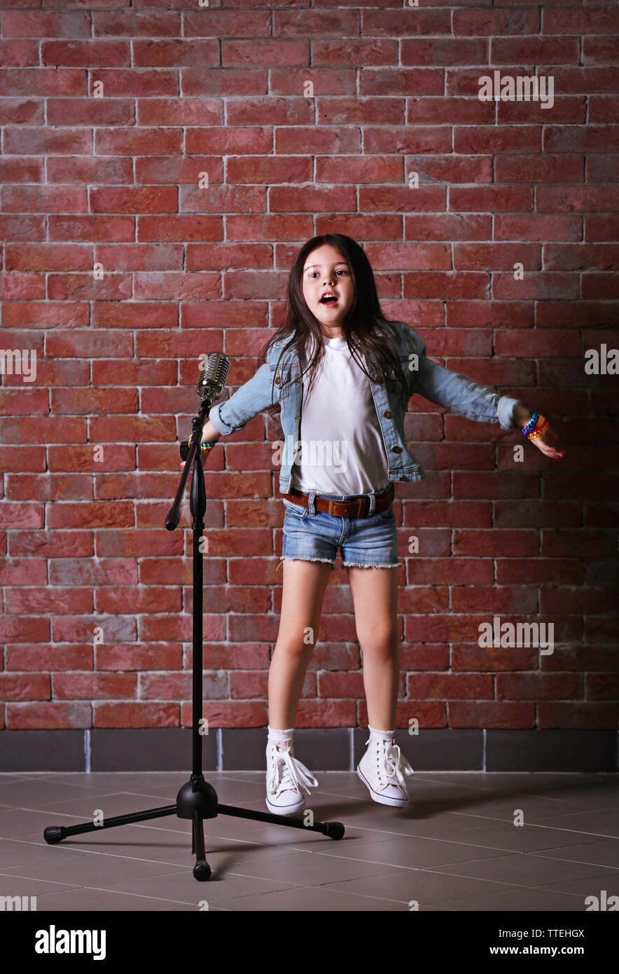 Beautiful little girl with microphone on brick wall background Stock ...