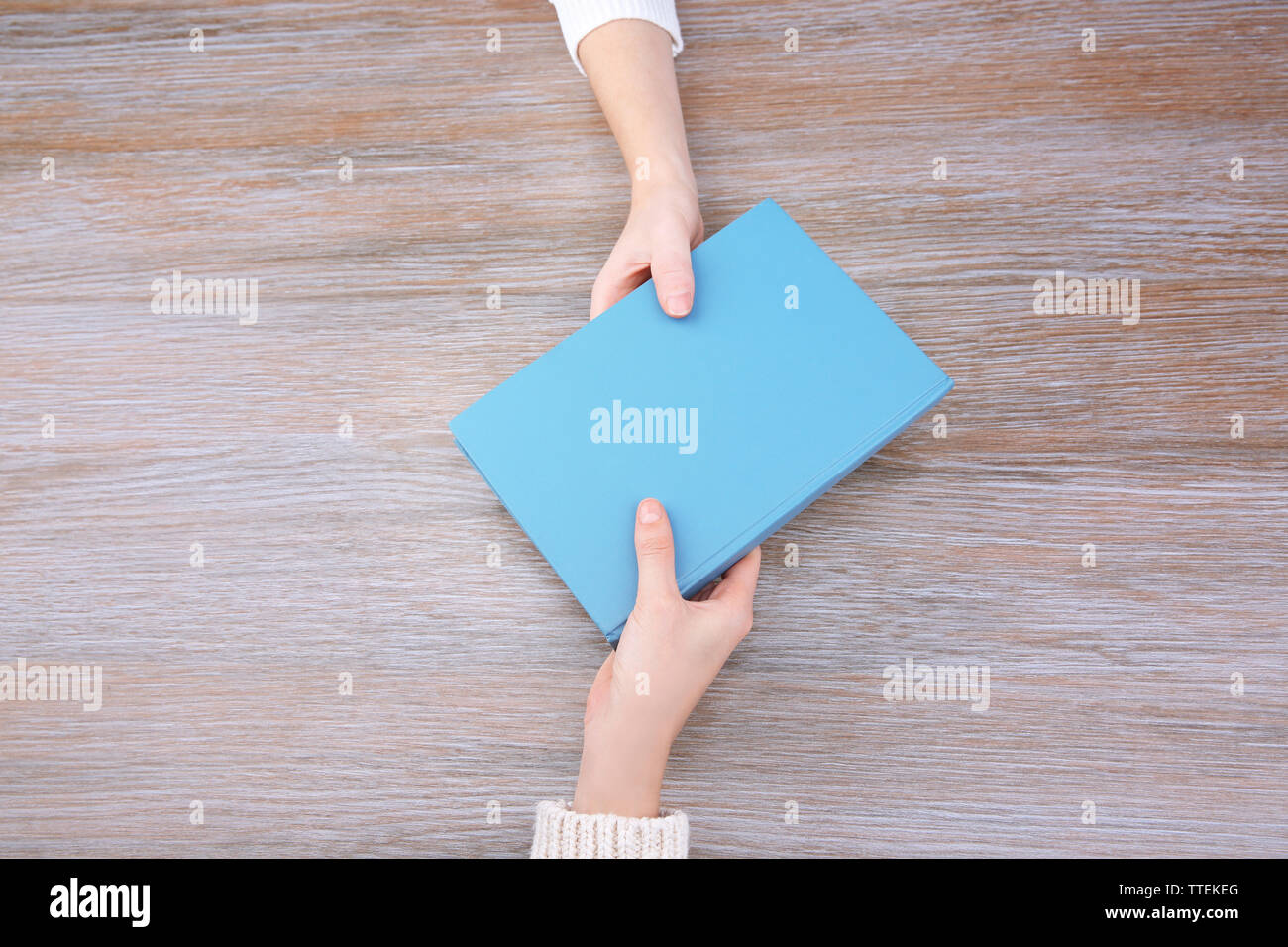 Woman giving book to woman, on wooden table background Stock Photo - Alamy