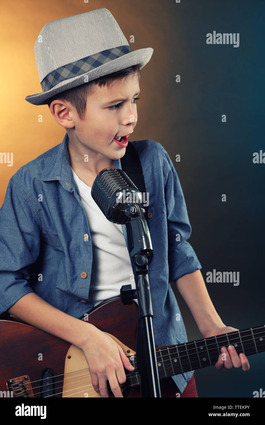 Little boy playing guitar and singing with microphone on a dark lighted ...